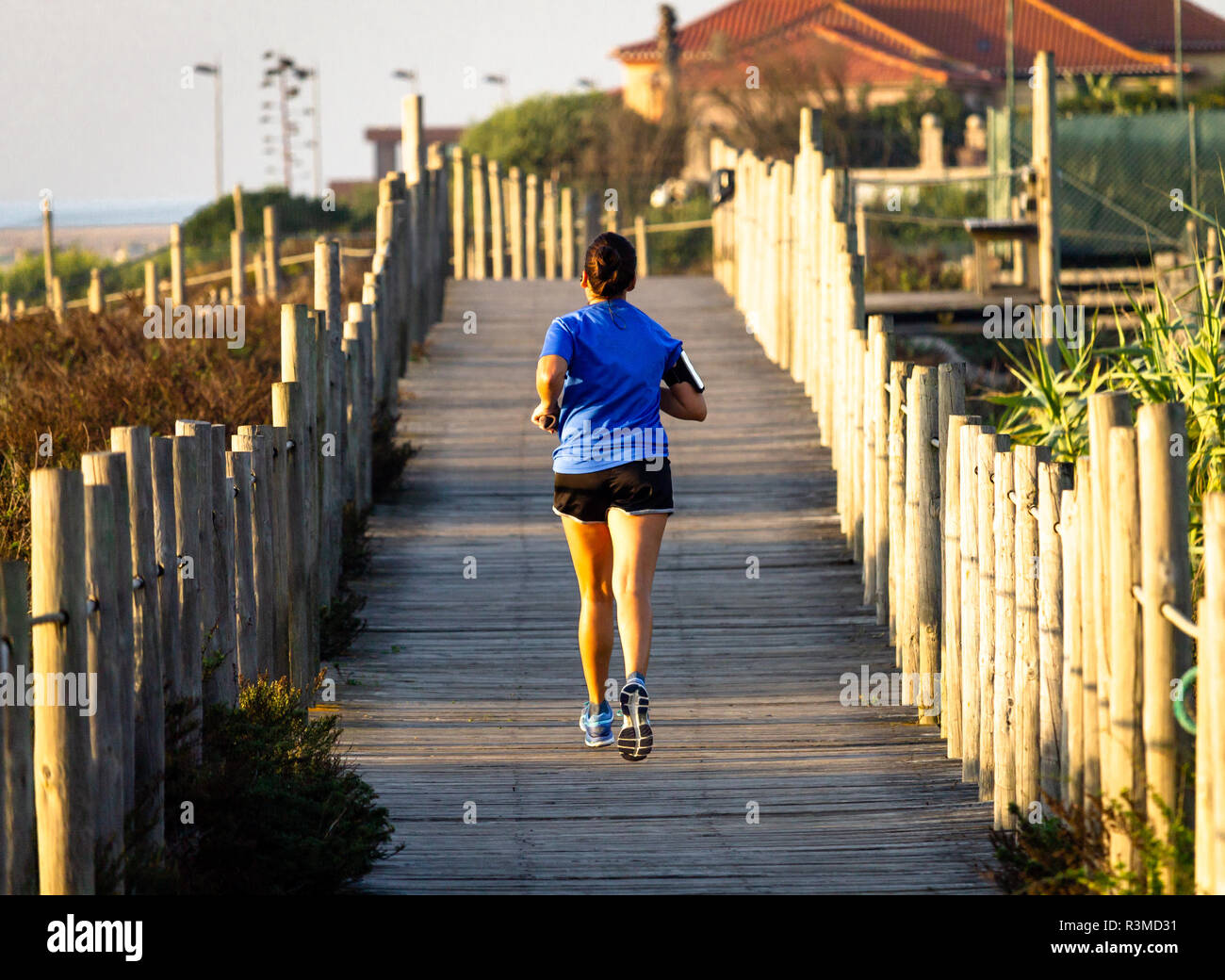 Young woman runs on boardwalk amidst vegetation. Blue t-shirt, black ...