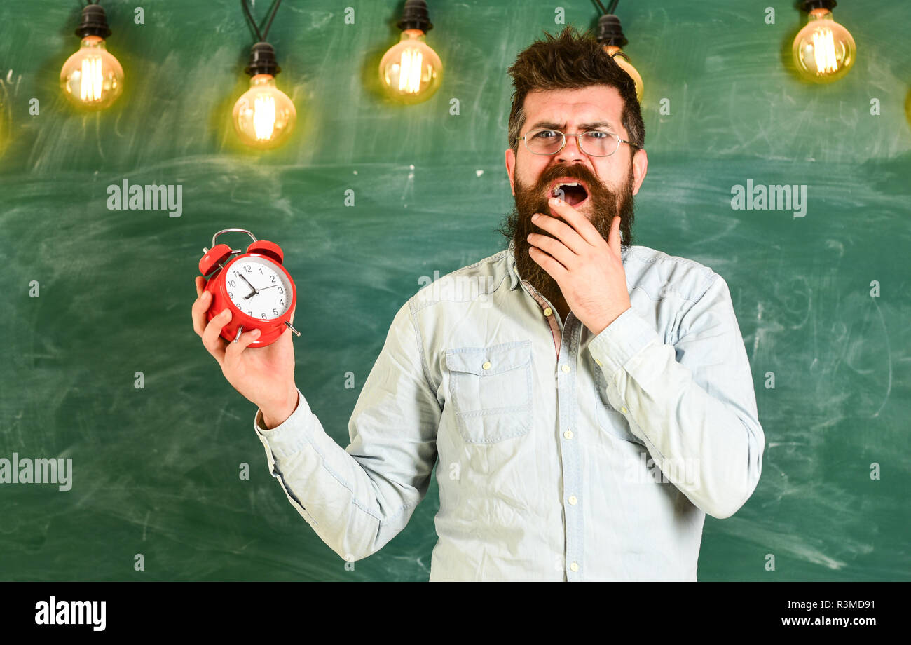 Forgot about time concept. Bearded hipster holds clock, chalkboard on ...