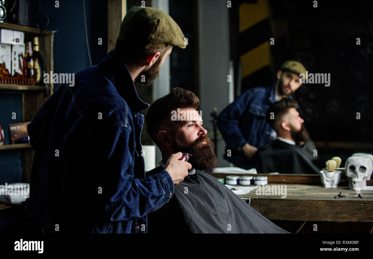 Barber busy with grooming beard of hipster client, mirror reflexion on ...