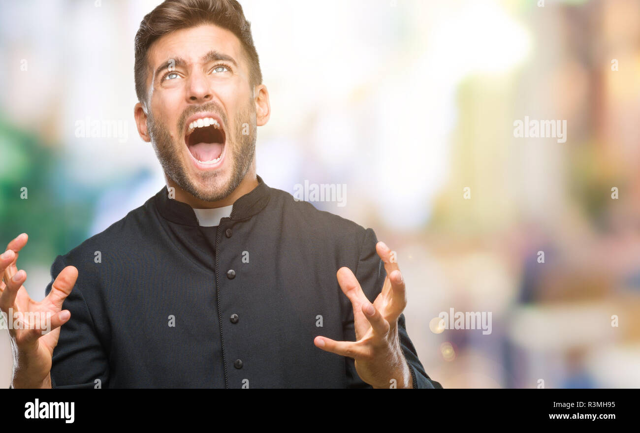 Young catholic christian priest man over isolated background crazy and ...