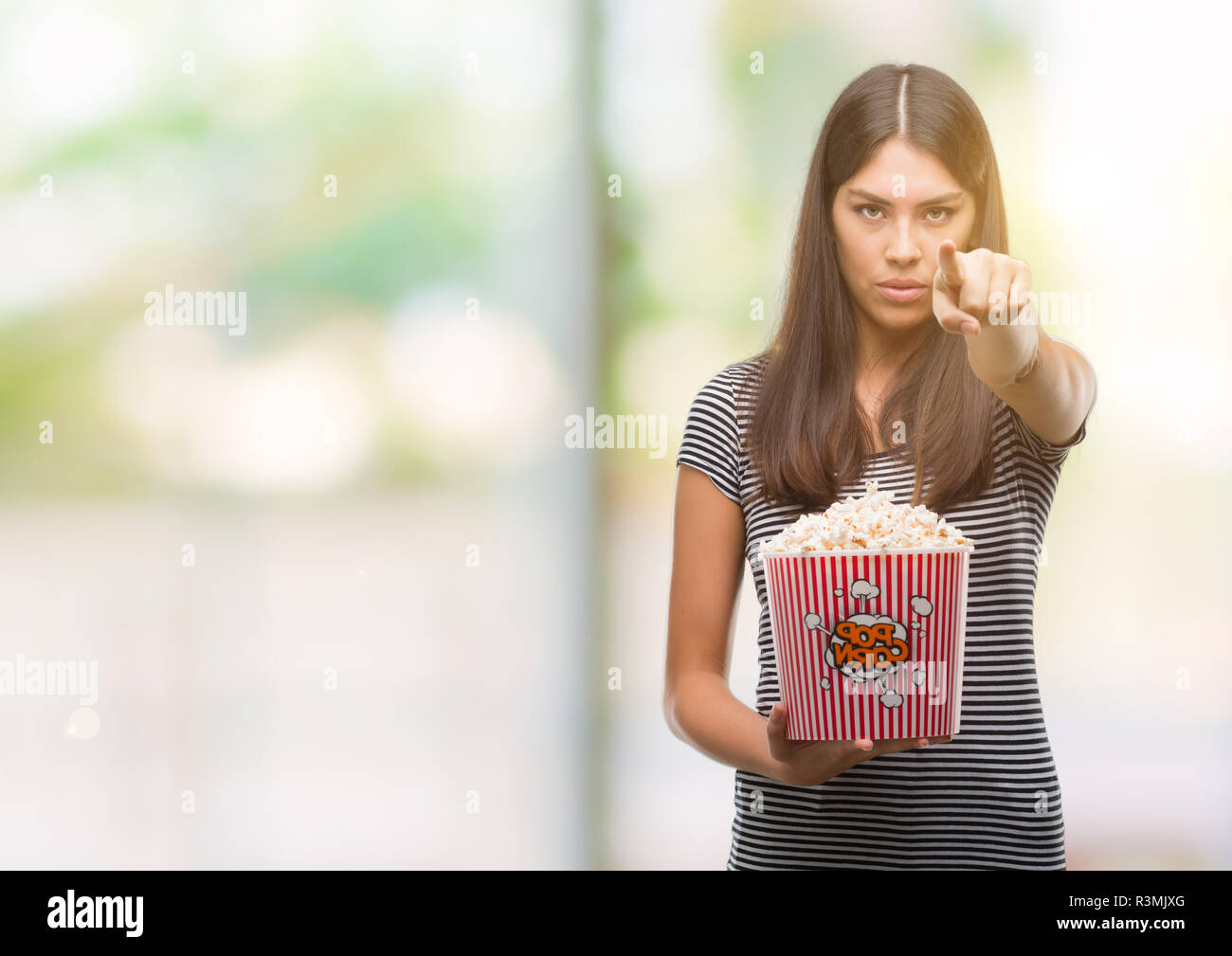 Young beautiful hispanic eating popcorn pointing with finger to the ...