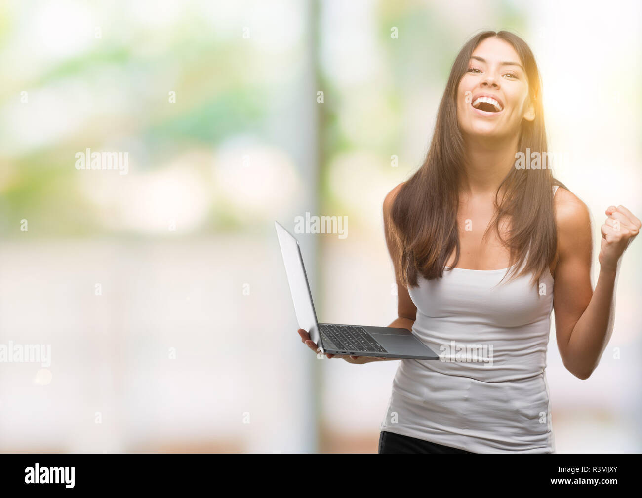 Young hispanic woman using computer laptop screaming proud and ...