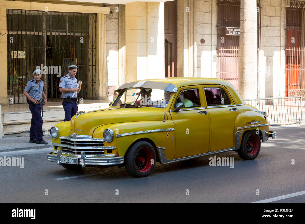 Cuba, Havana. Classic yellow car passing two policemen on sidewalk ...