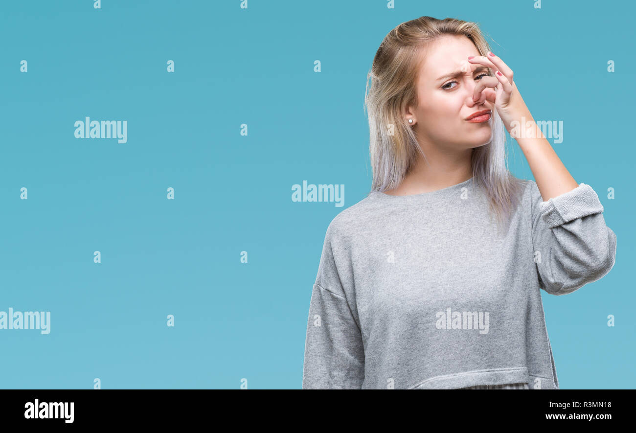Young blonde woman over isolated background smelling something stinky ...