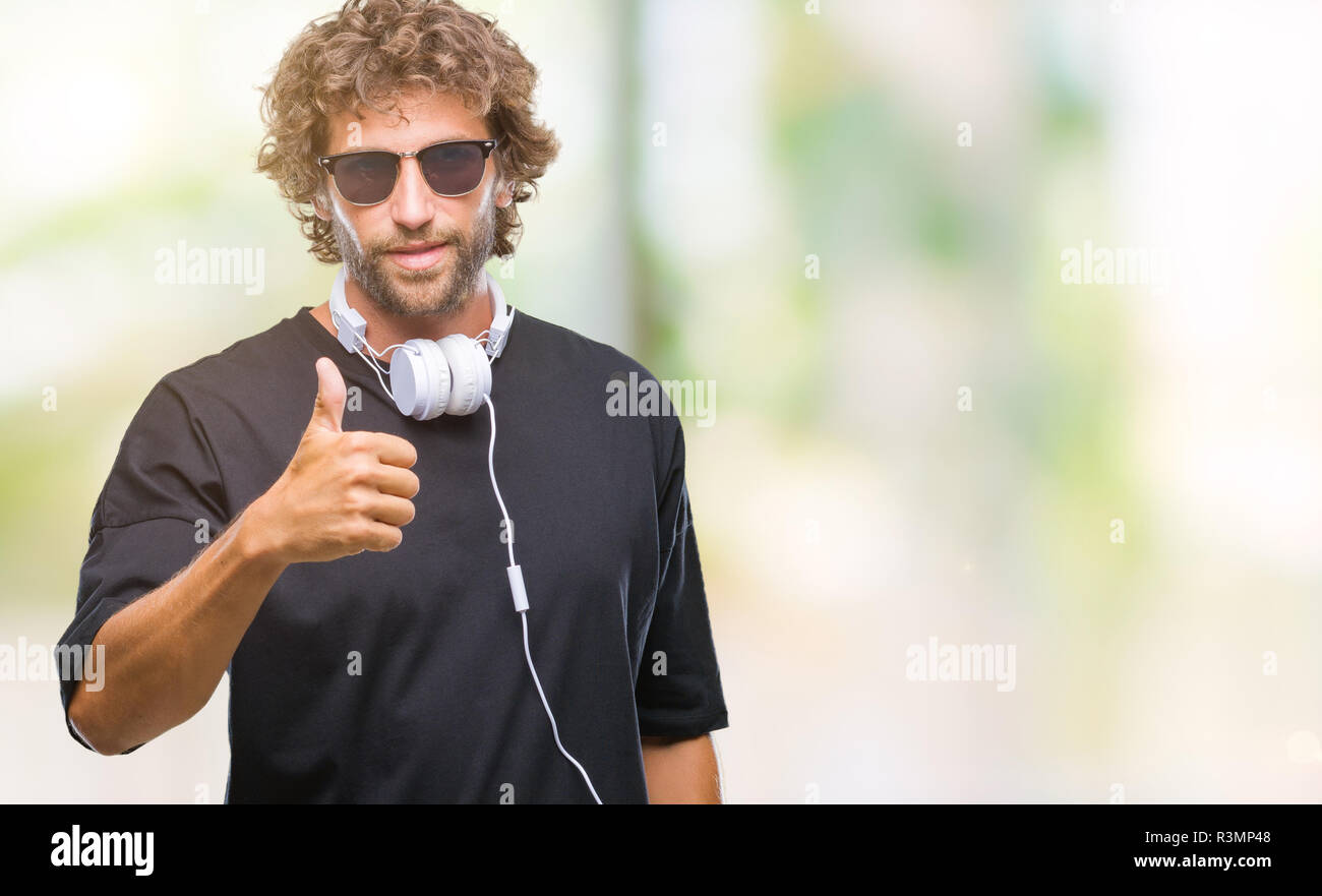 Handsome hispanic man listening to music wearing headphones over ...
