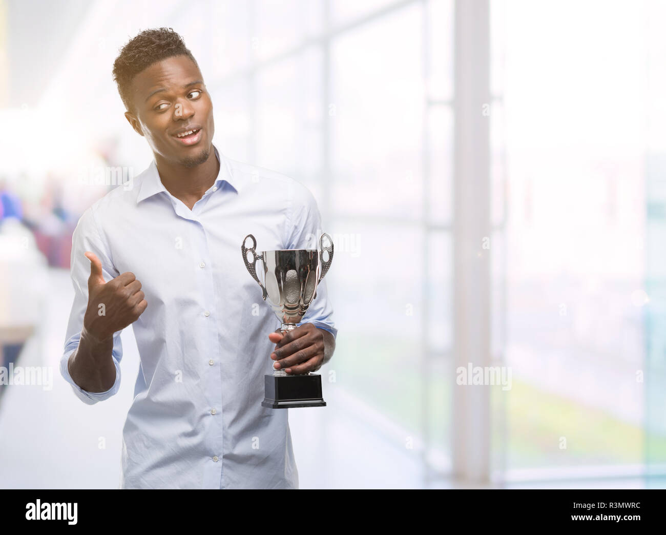 Young african american man holding trophy pointing with hand and finger ...