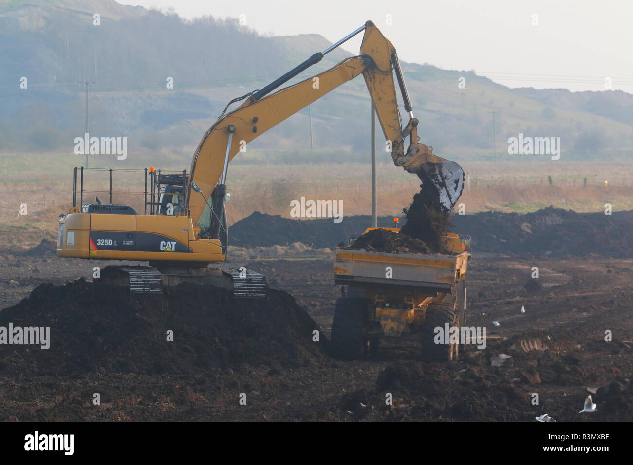 A Caterpillar 325 backhoe loading dump trucks on the construction of ...