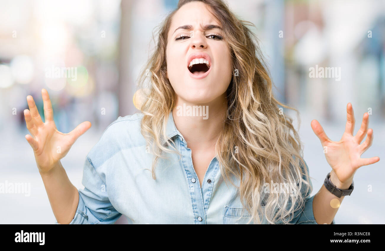 Beautiful young blonde woman over isolated background crazy and mad ...