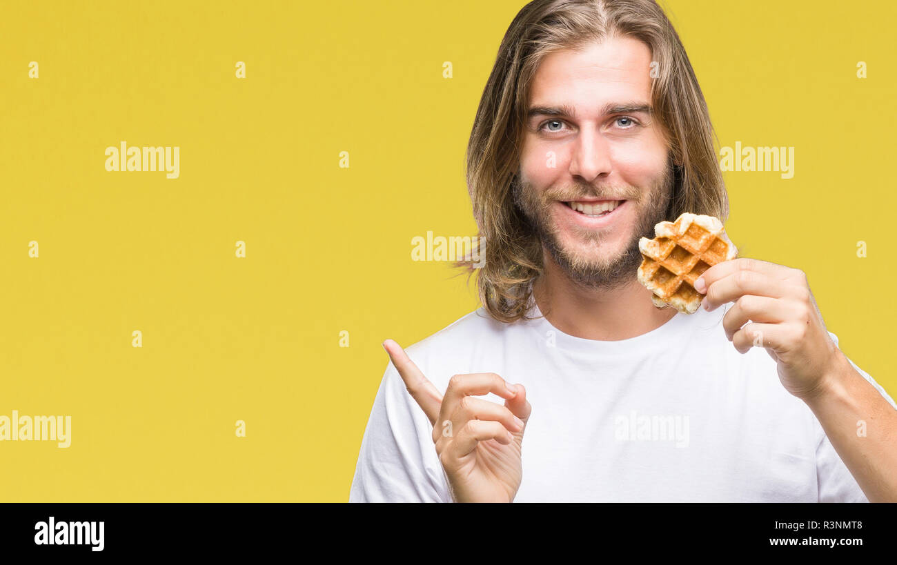 Young handsome man with long hair over isolated background eating ...