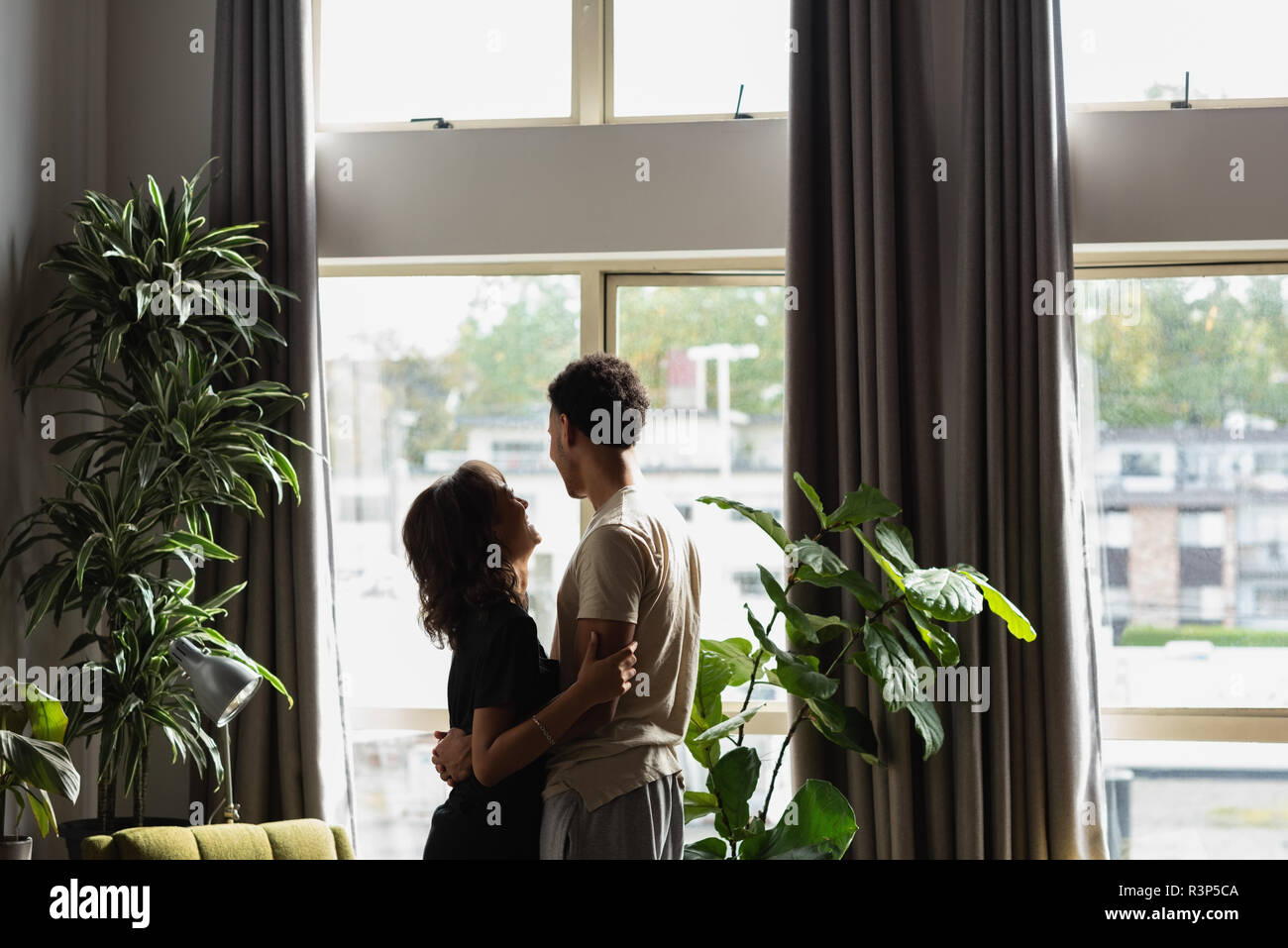 Couple looking through window in living room Stock Photo - Alamy