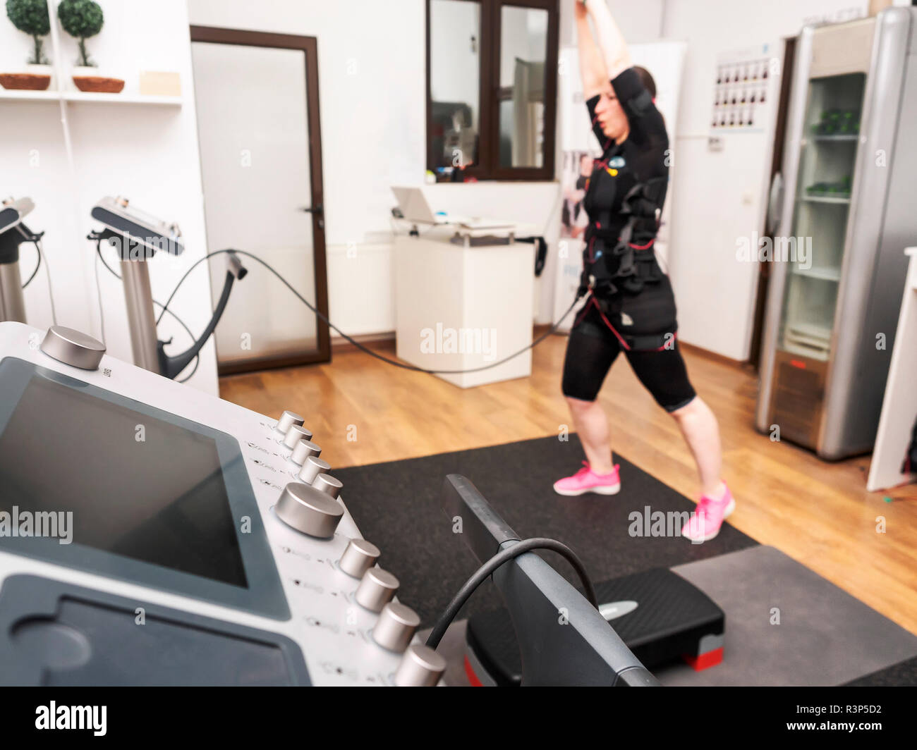 Young woman at the gym by training in a suit with electric impulses ...