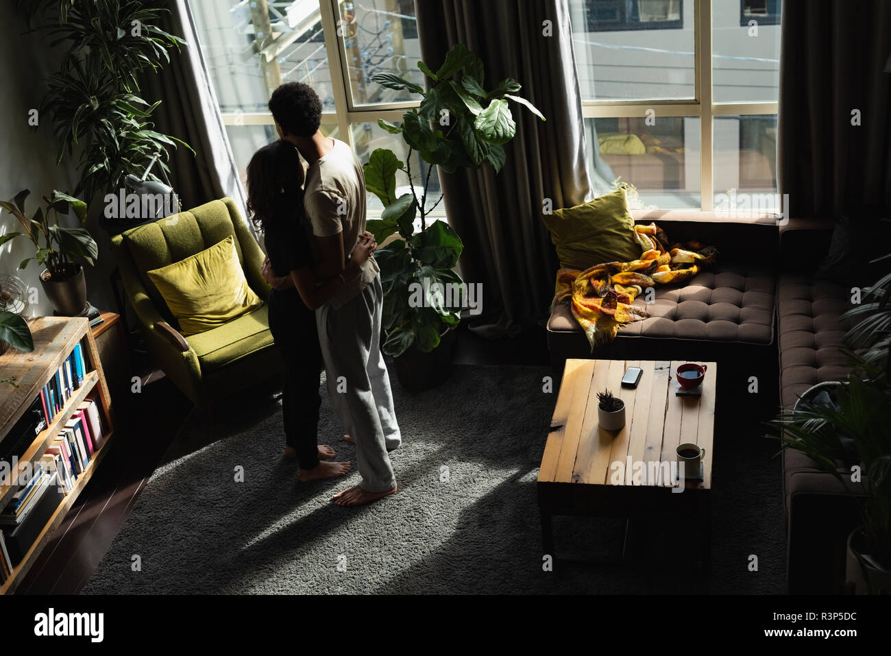 Couple looking through window in living room Stock Photo - Alamy