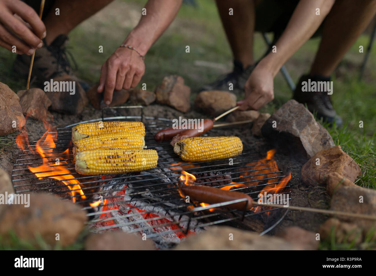 Men roasting sausage and corn on campfire at campsite Stock Photo - Alamy