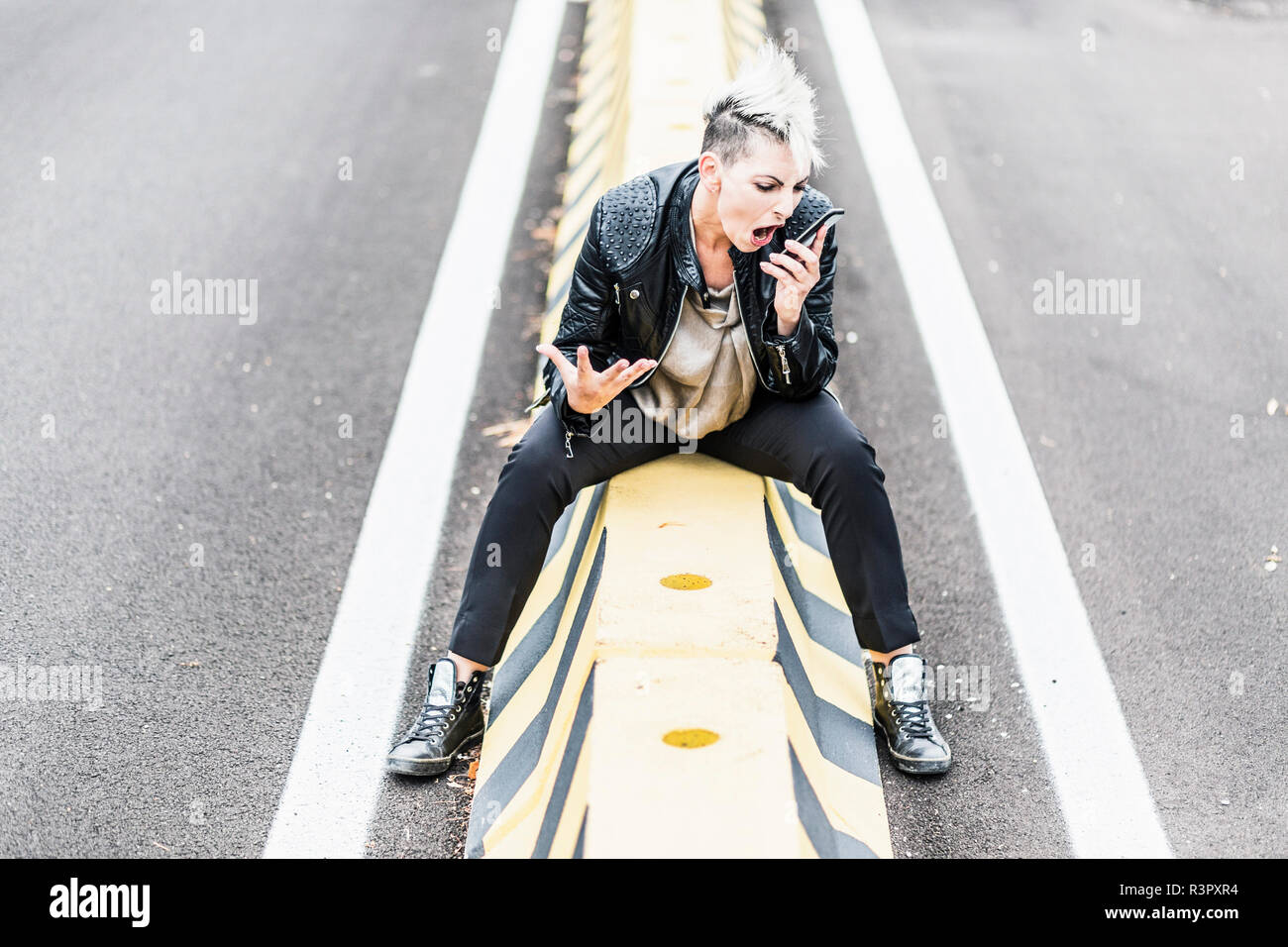 Aggressive punk woman sitting at the roadside screaming into cell phone ...