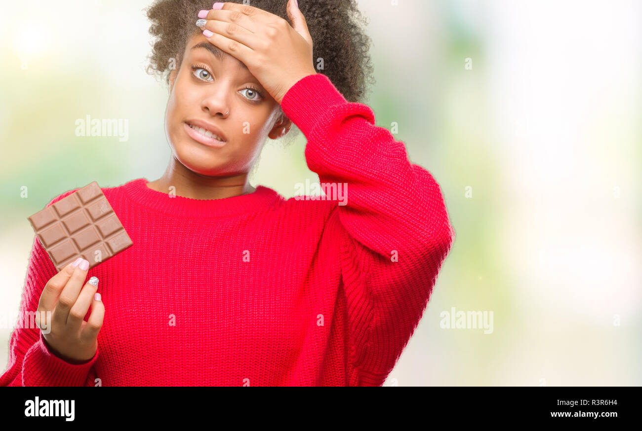 Young afro american woman eating chocolate bar over isolated background ...
