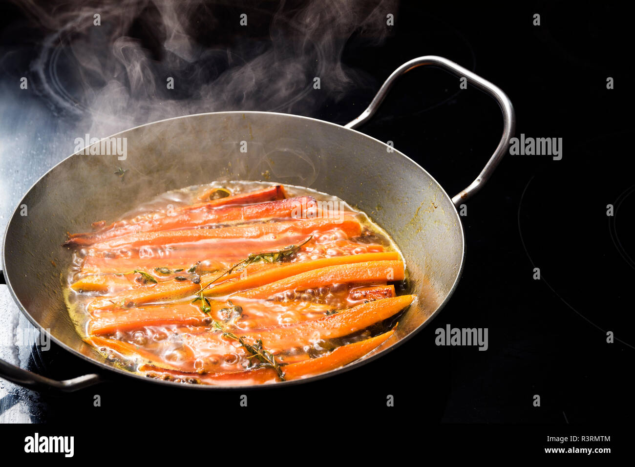 cooking carrots with herbs and spices in a steaming wok pan on the ...
