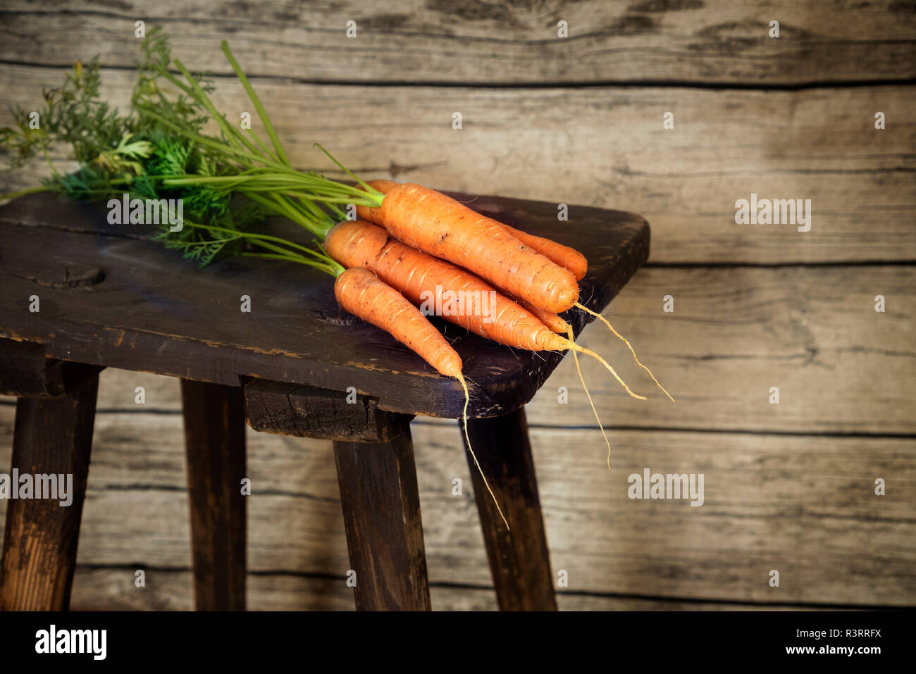 organic carrots on an old stool in front of a rustic wooden wall with ...
