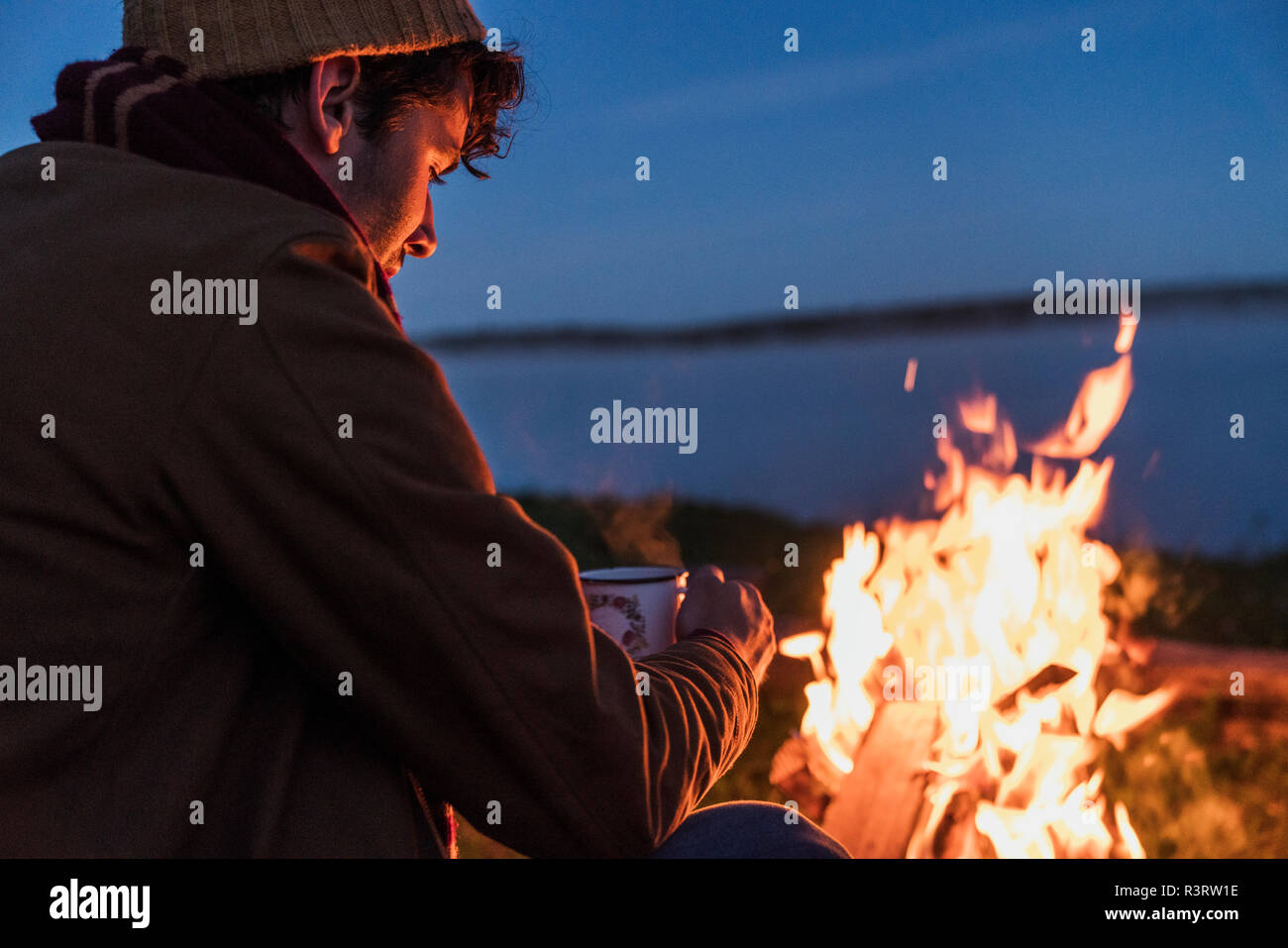 Young man sitting at a campfire, watching the flames Stock Photo - Alamy