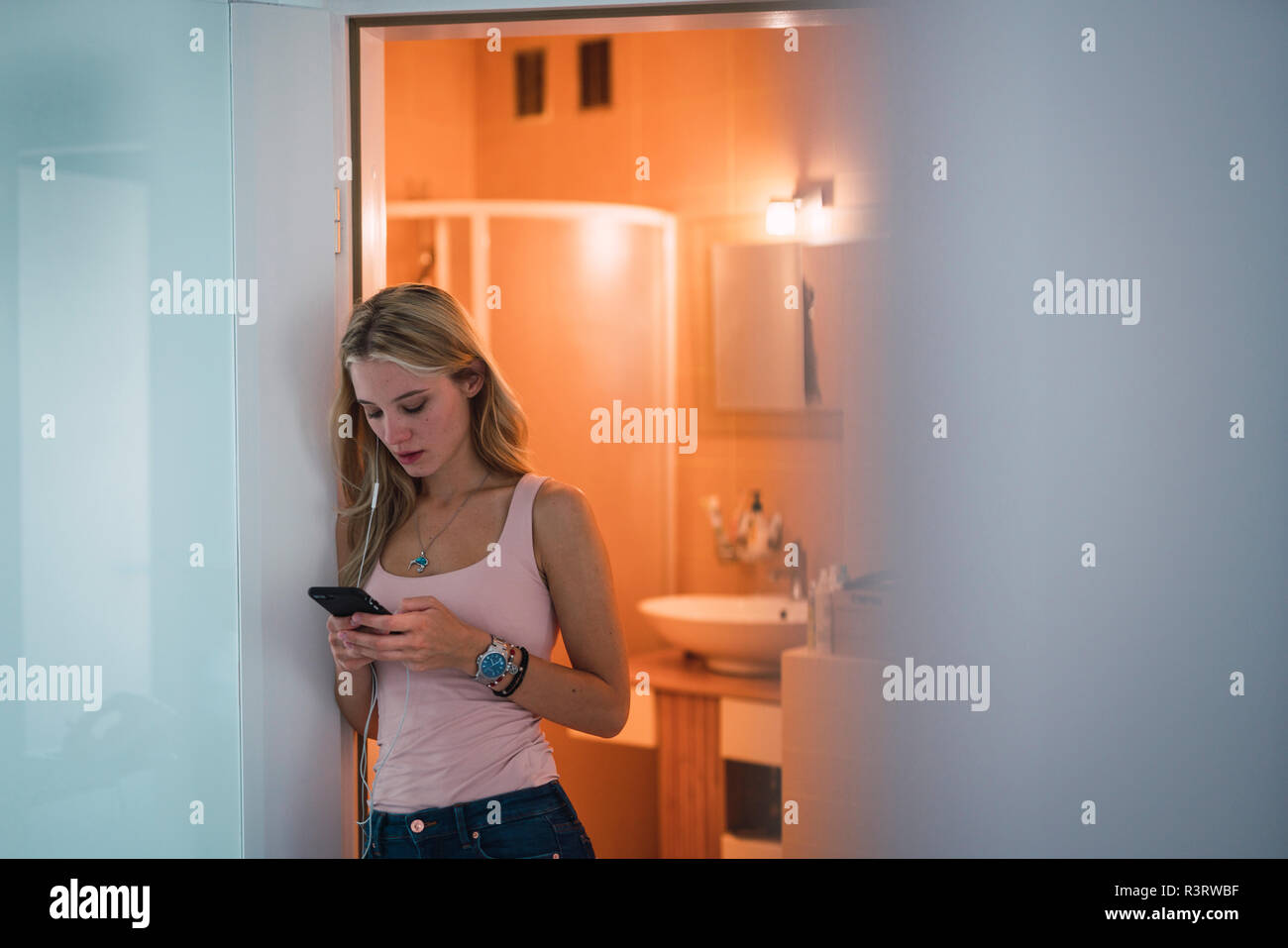 Blond young woman checking cell phone at home Stock Photo - Alamy