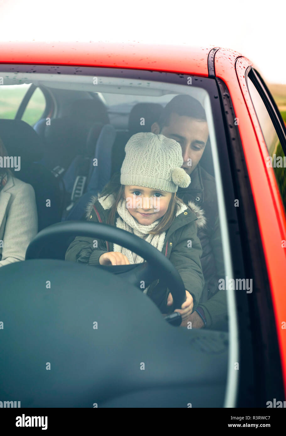Little girl with wool cap driving car sitting on father's lap Stock ...