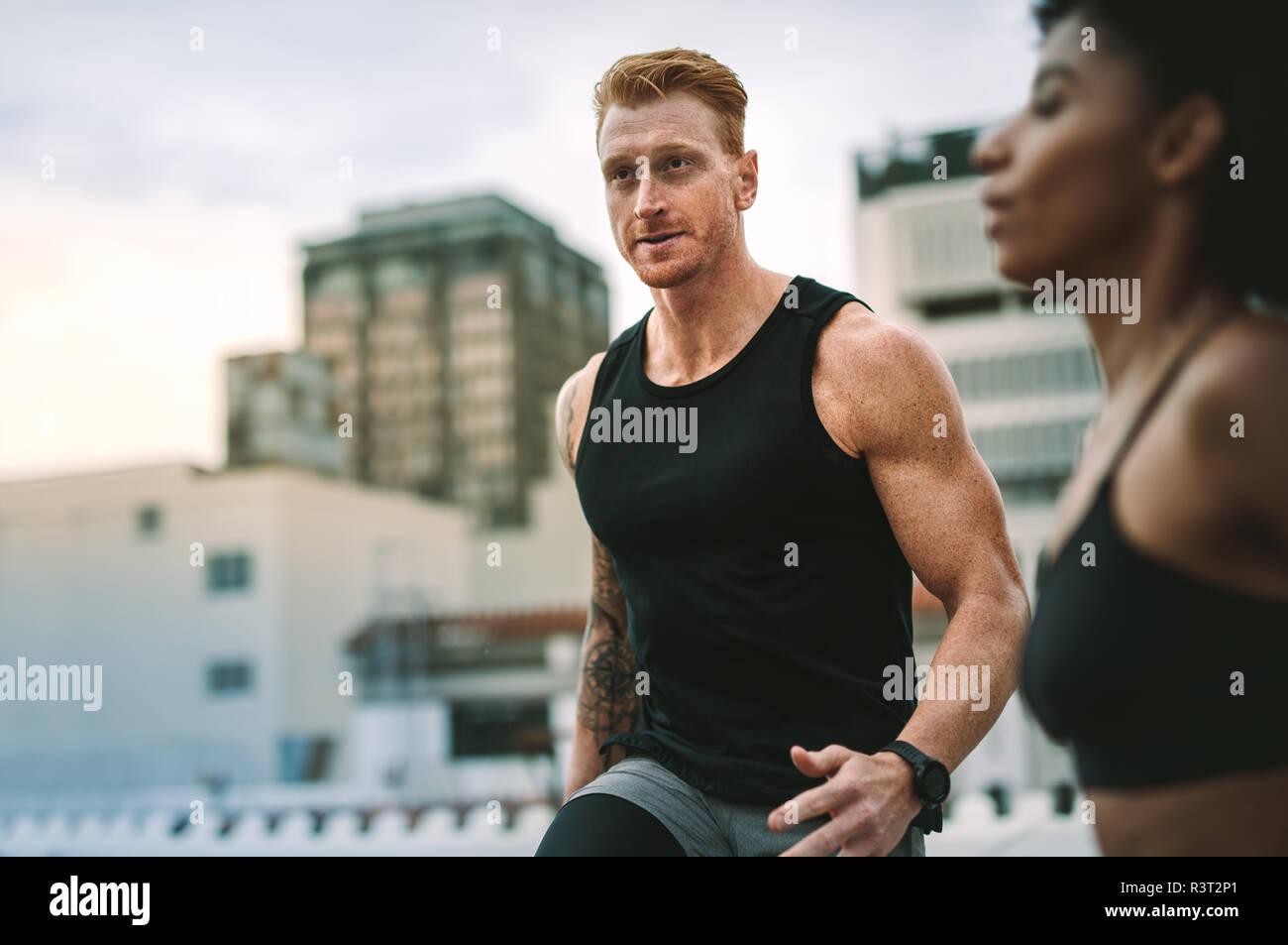 fitness man and woman doing workout on a rooftop with high rise ...