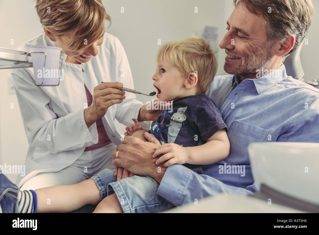 Female dentist examining little boy, sitting on his father's lap Stock ...