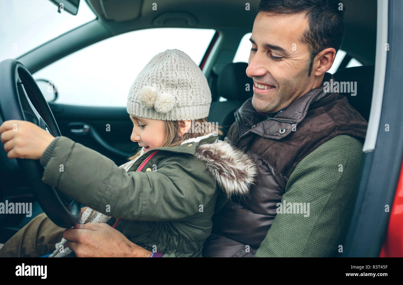 Happy little girl with wool cap driving car sitting on father's lap ...