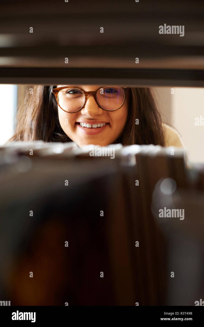Portrait of smiling young student looking through bookshelf in the ...