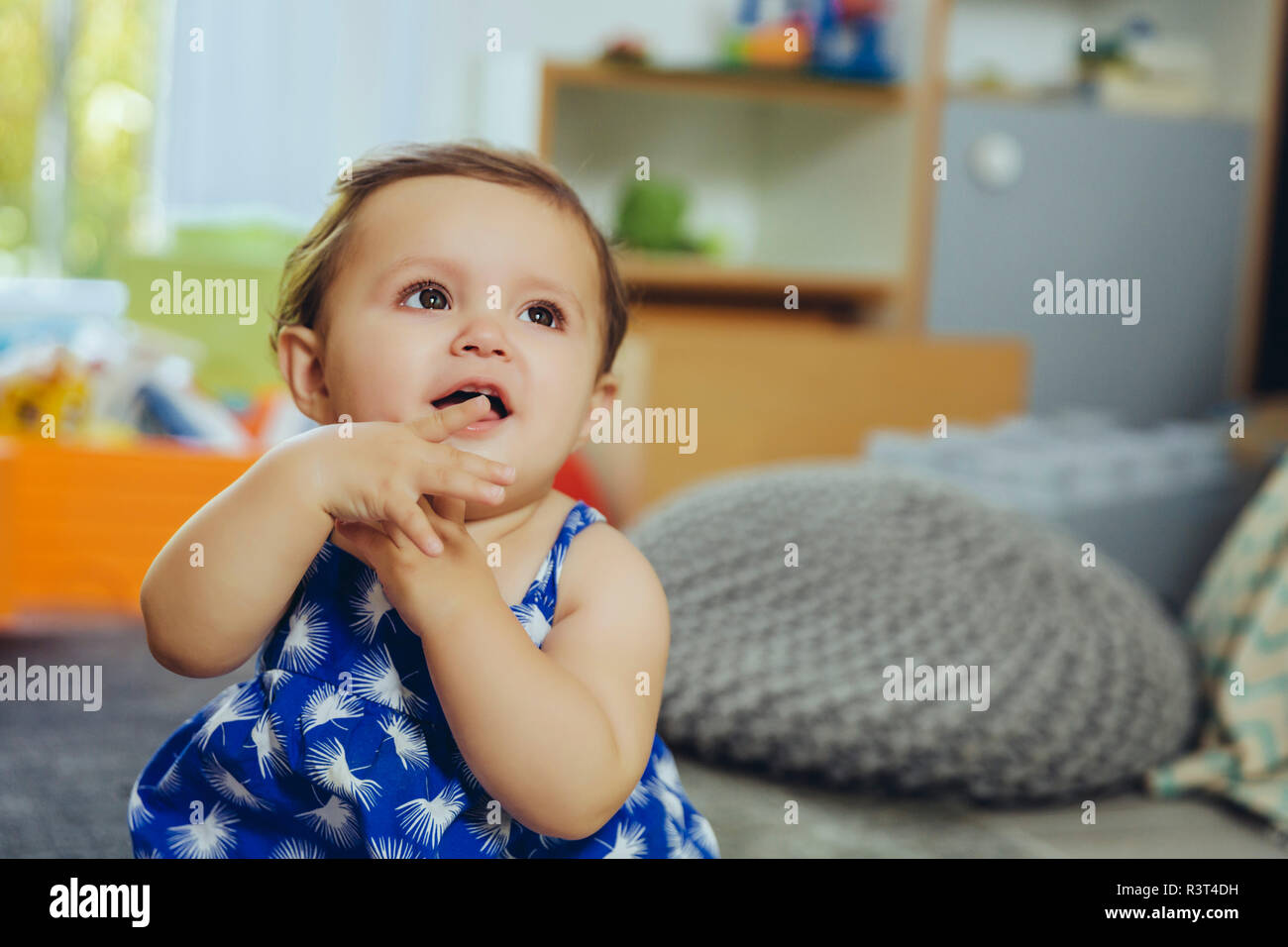 Baby girl sitting at home looking up Stock Photo - Alamy