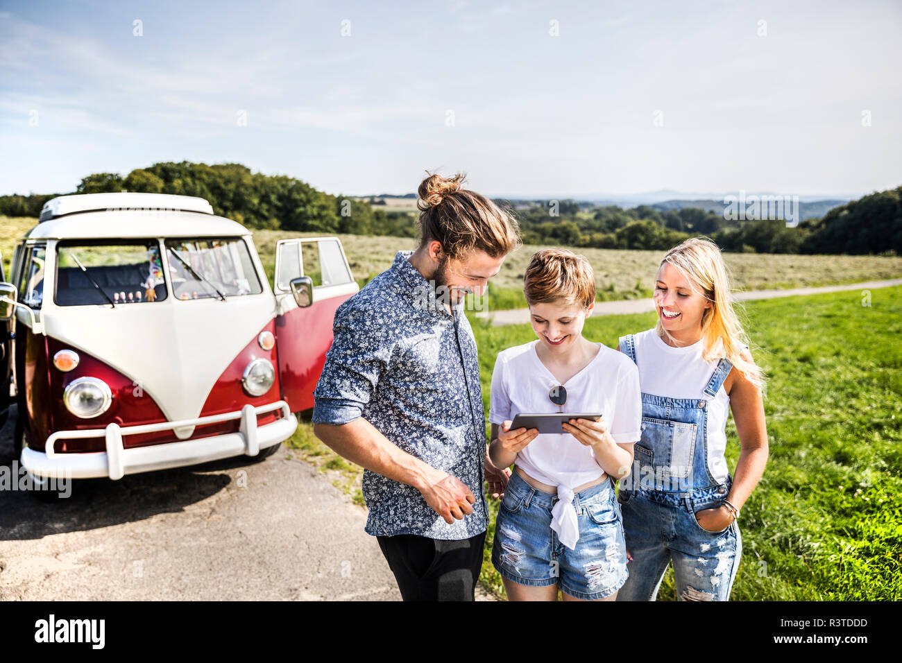 Happy friends outside van in rural landscape looking at tablet Stock ...