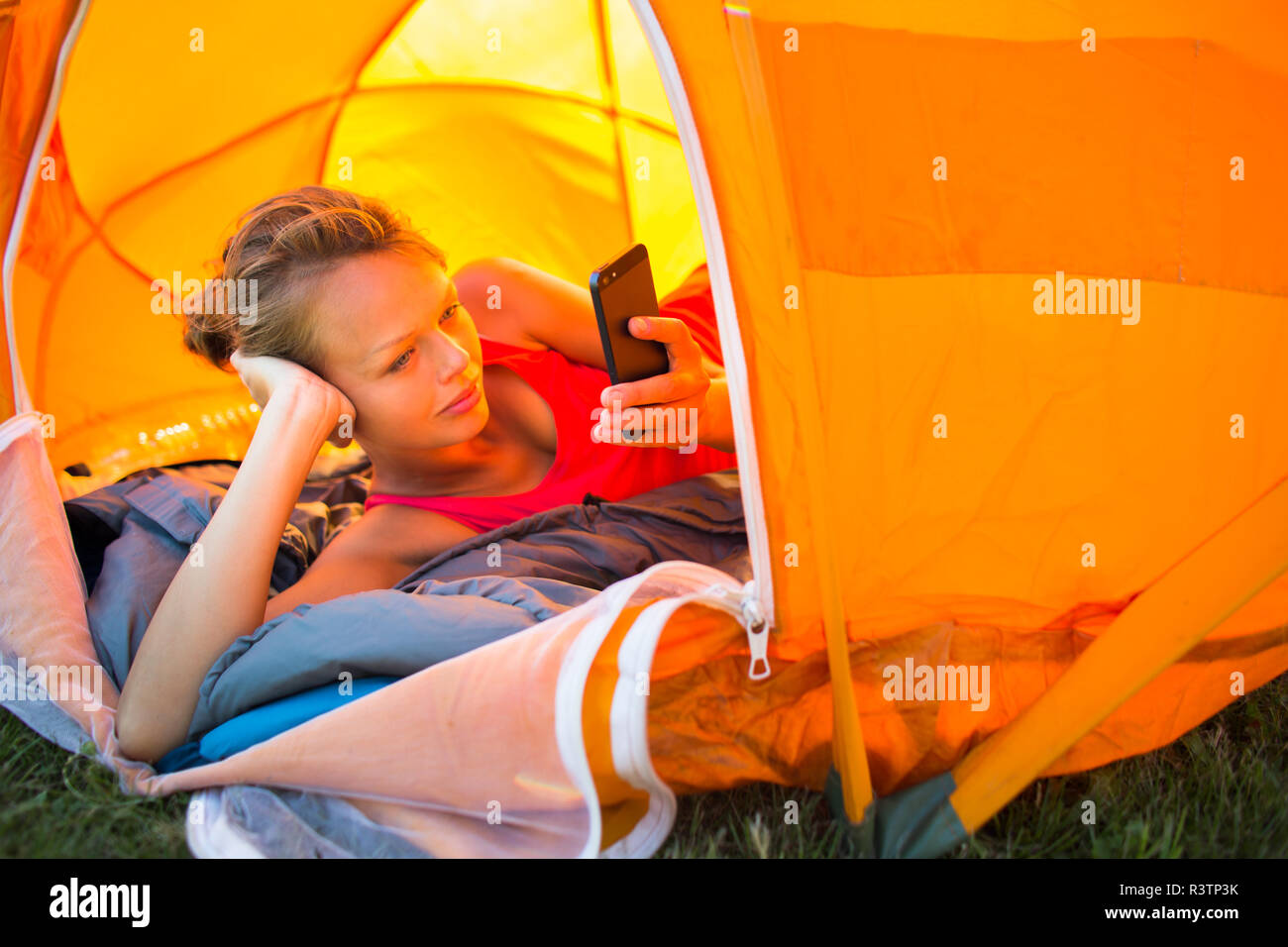 Pretty, young woman camping outdoors, lying in the tent in the morning ...