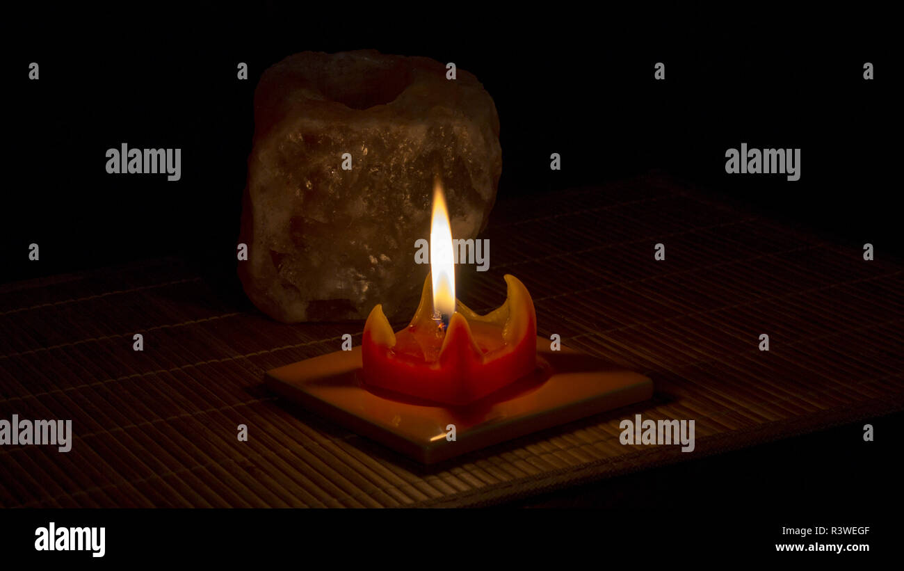 The flame of a red candle illuminates the stone salt tea light lamp on ...