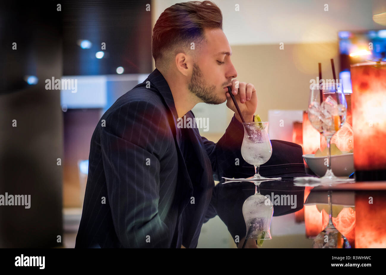 Handsome young man drinking cocktail at bar counter, wearing business ...