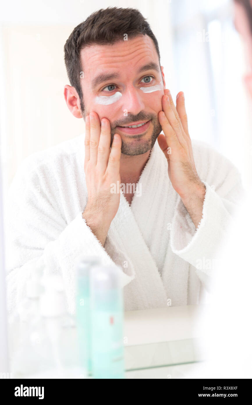 Young attractive man applying anti dark circles cream around eyes Stock ...