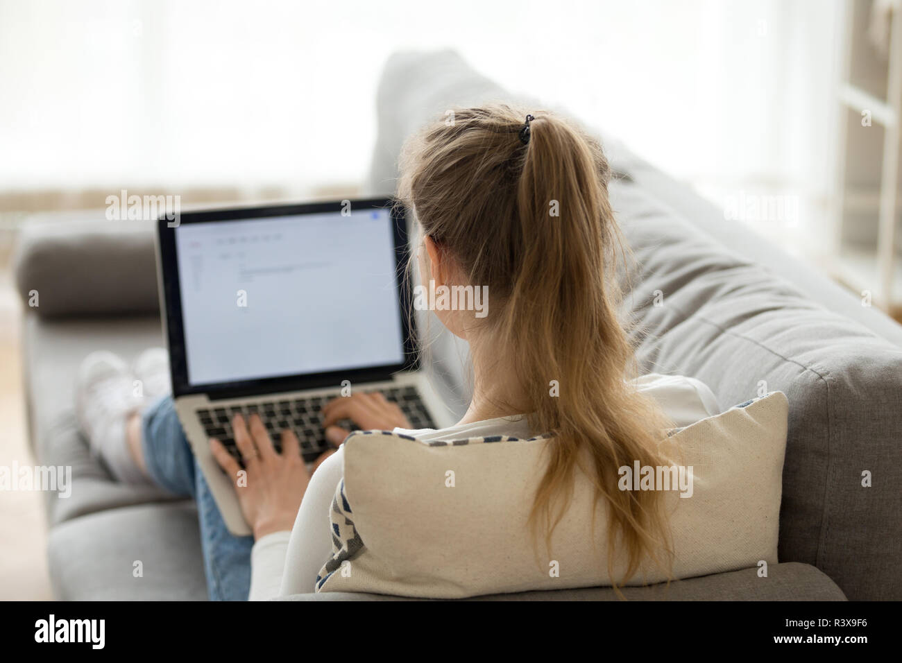 Back view of female lying on couch texting on laptop Stock Photo - Alamy