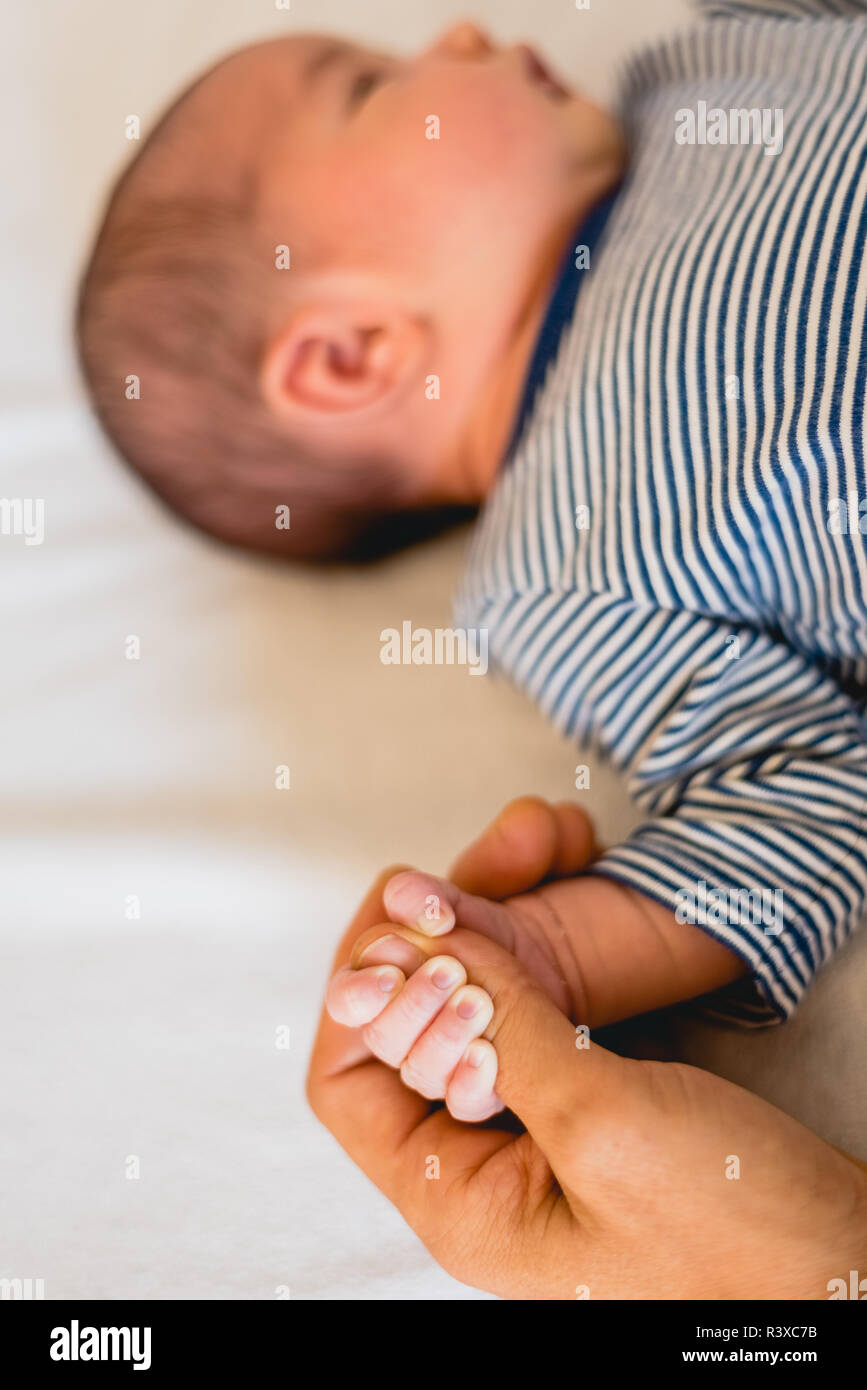 Newborn baby securely grasping his mother's hands, close-up fingers ...
