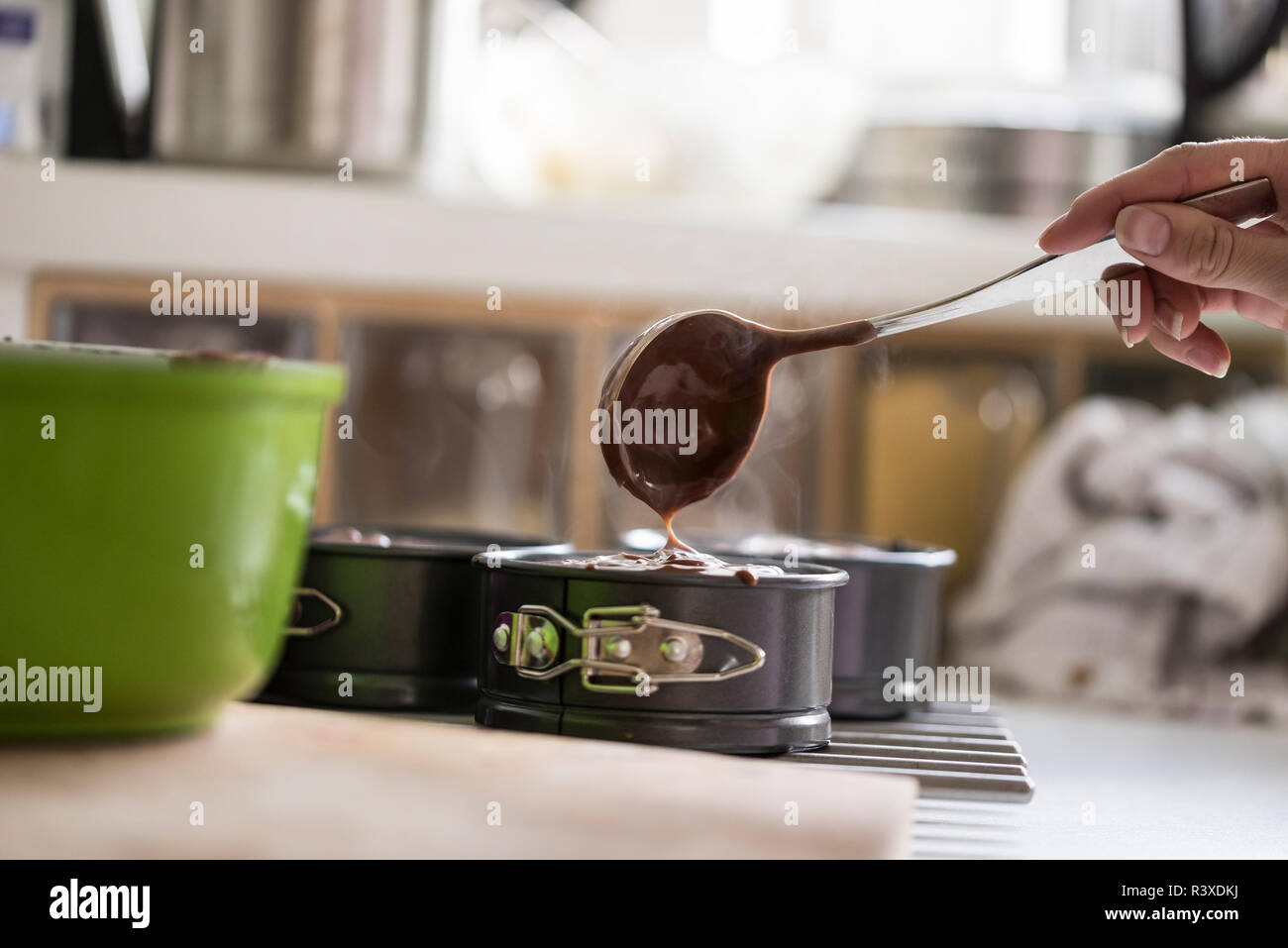 Woman filling baking tins with chocolate cake mix spooning it in with a ...