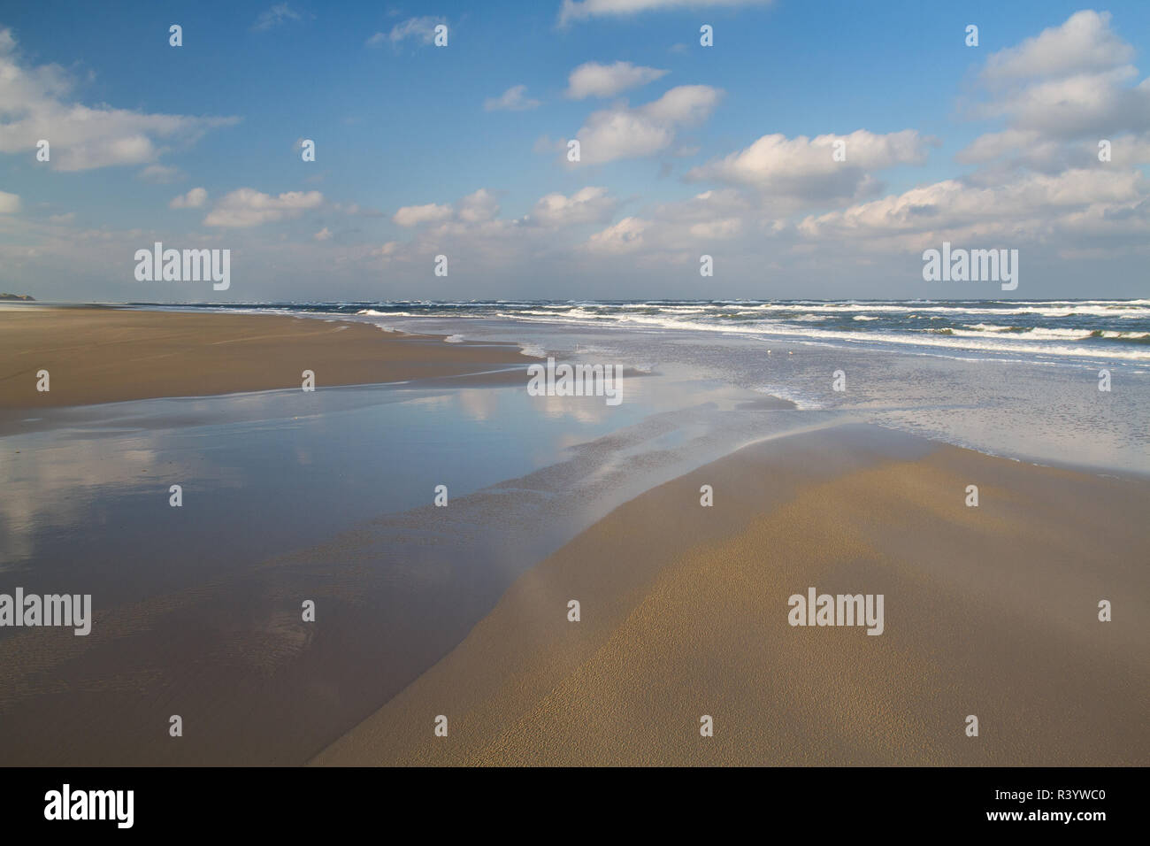 Vast beach at ebb tide, blue sky and white clouds reflected in the ...