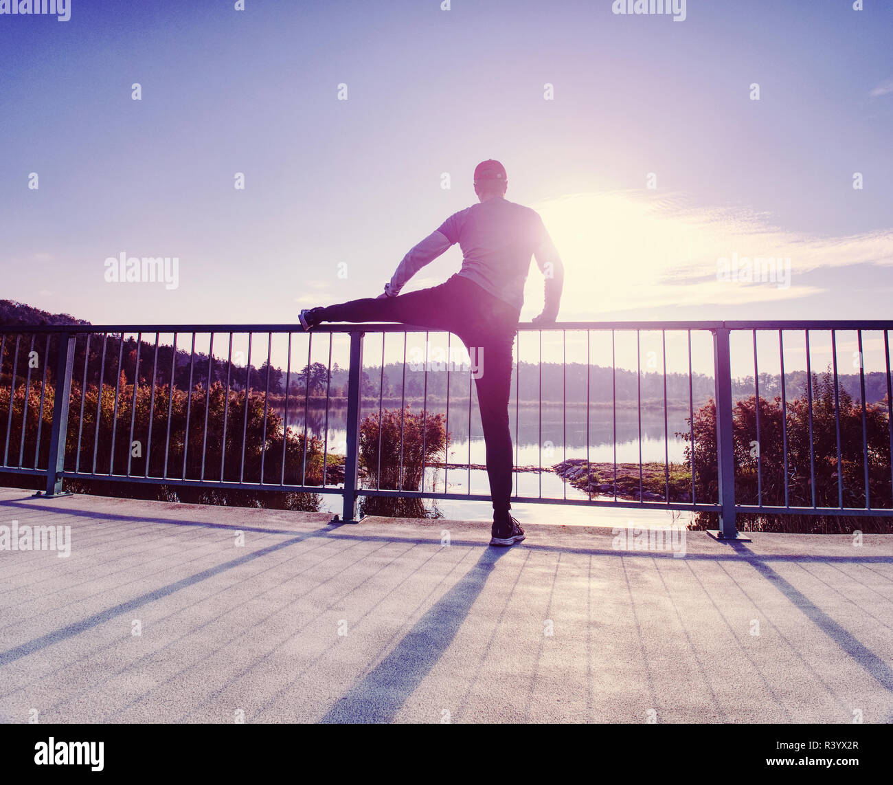 Runner doing stretching exercise on bay bridge. An active wiry man ...