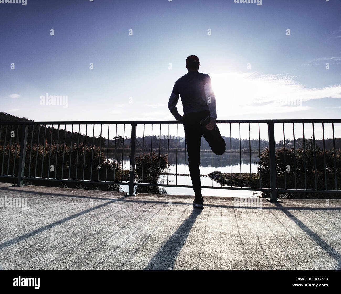 Man is stretching legs in break from run. The Sun is outlining man body ...