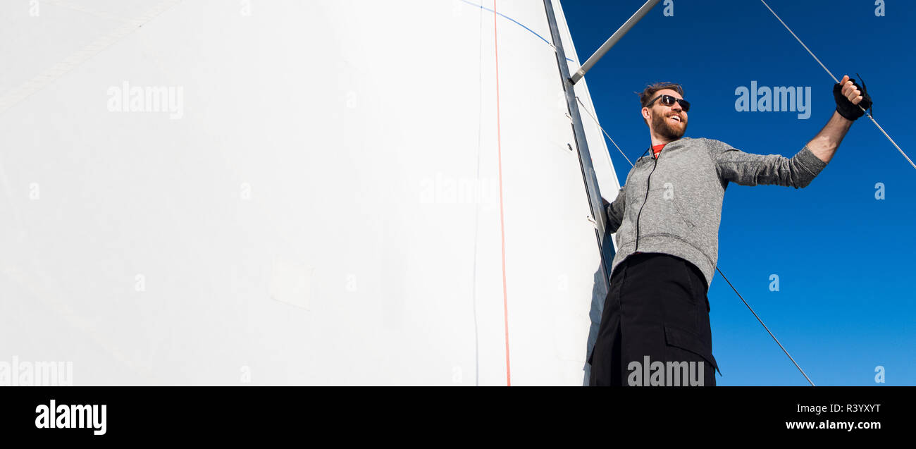 Yacht captain with a beard stands on sail boom on a sailing yacht ...