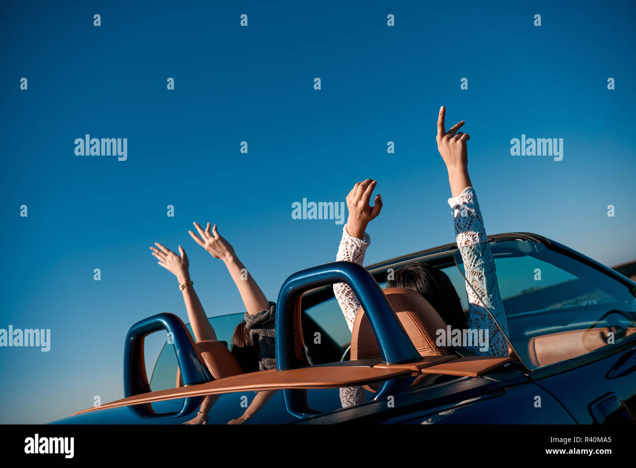 Female friends driving cabriolet with the hands up and having fun on ...