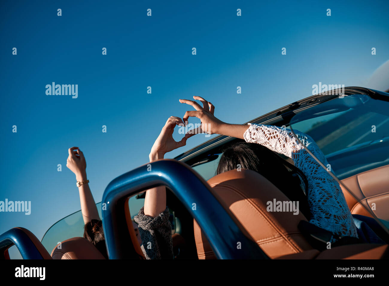 Female friends driving cabriolet with the hands up and having fun on ...