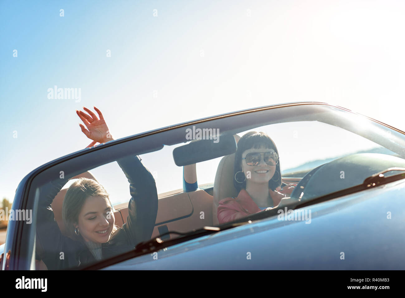 Female friends driving cabriolet with the hands up and having fun on ...