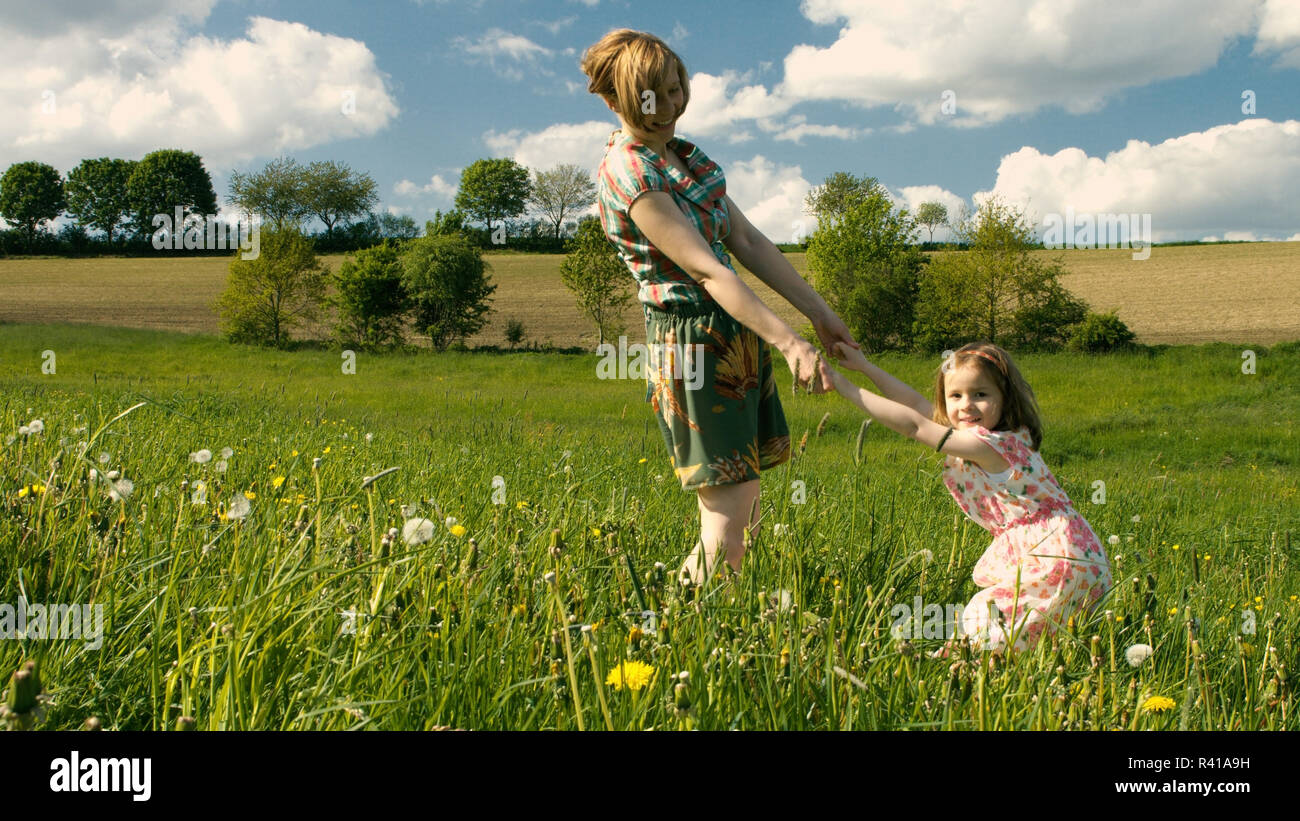mother and daughter dance together in the wind on a spring meadow ...