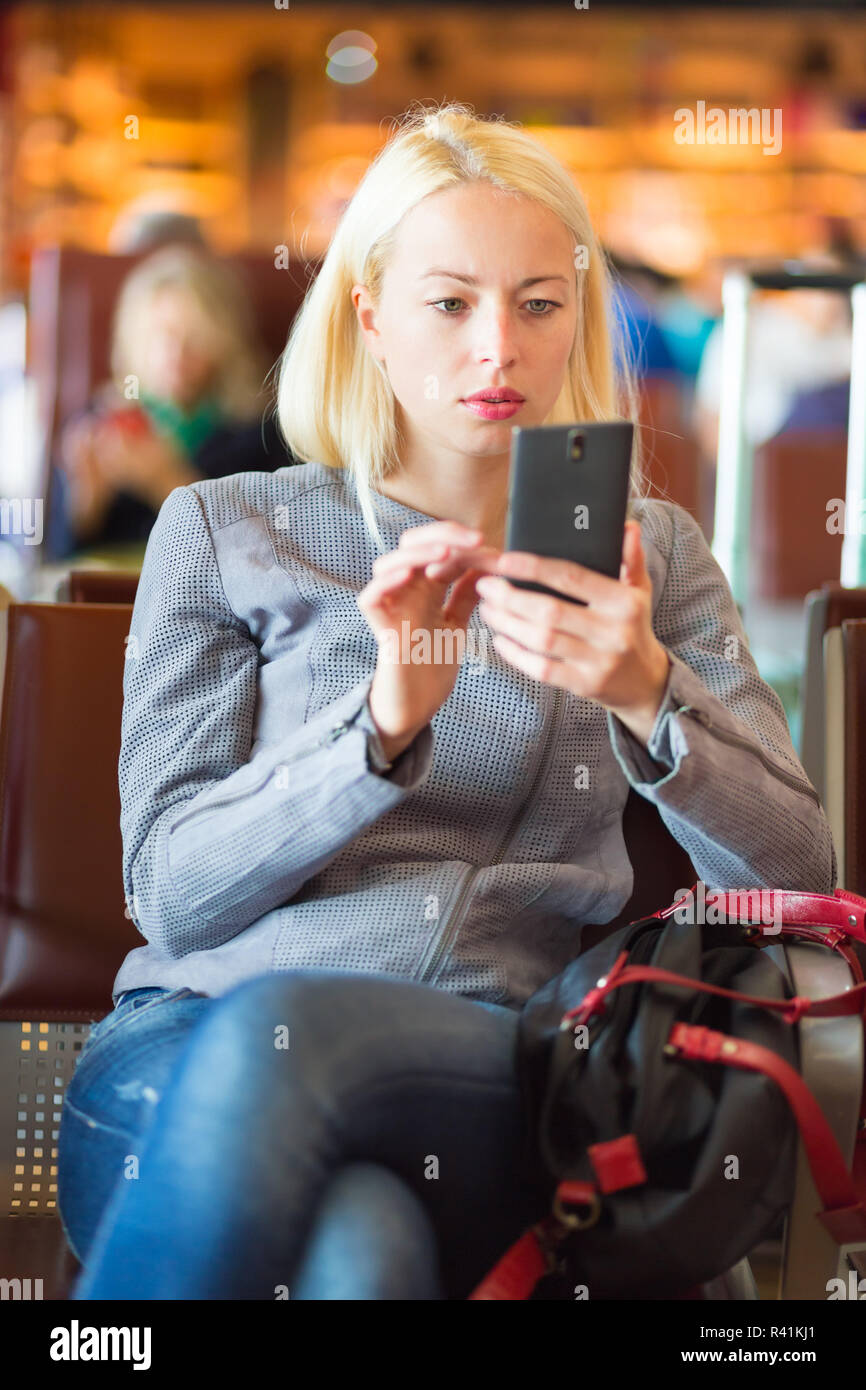 Female traveler using cell phone while waiting Stock Photo - Alamy