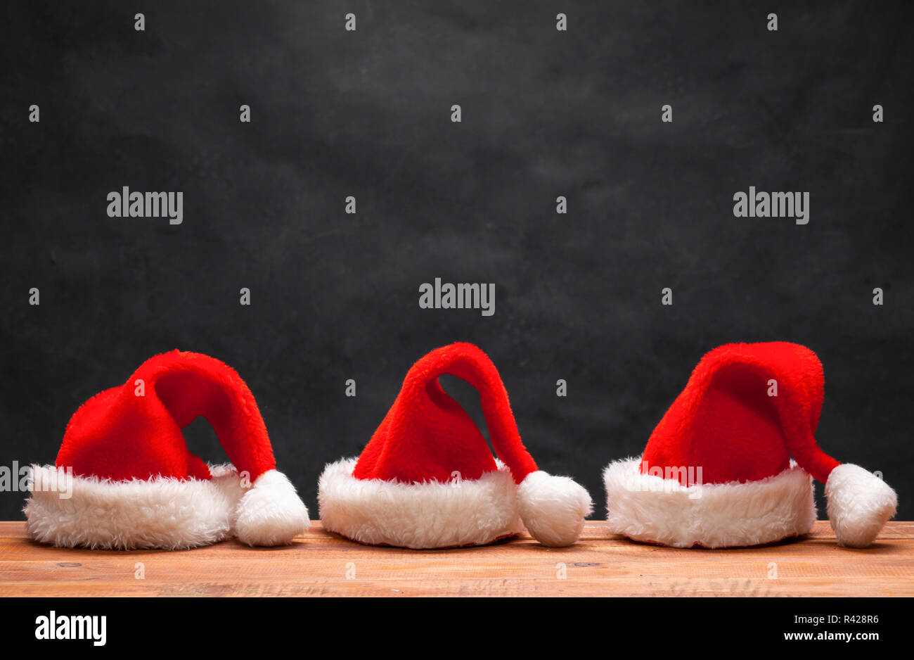 The three Santa red hats on wooden background Stock Photo - Alamy