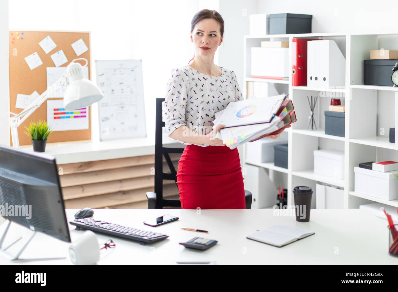 A young girl stands near a computer Desk in the office and holds ...