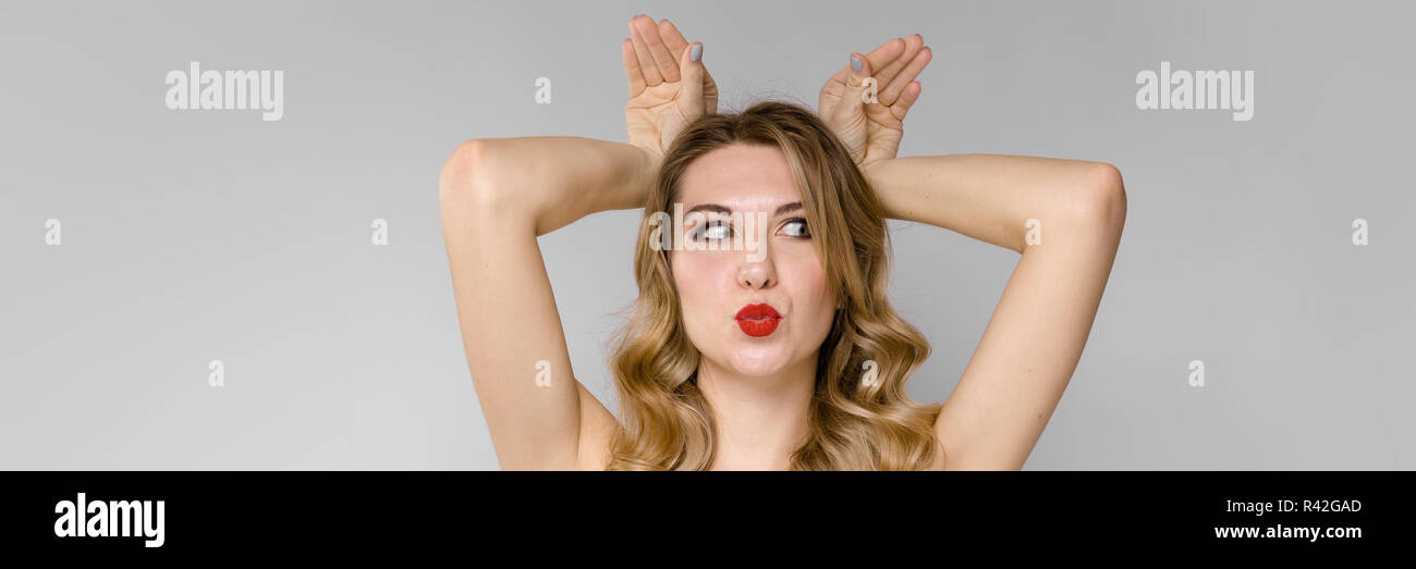 A young beautiful girl fools by putting two hands on her head and ...