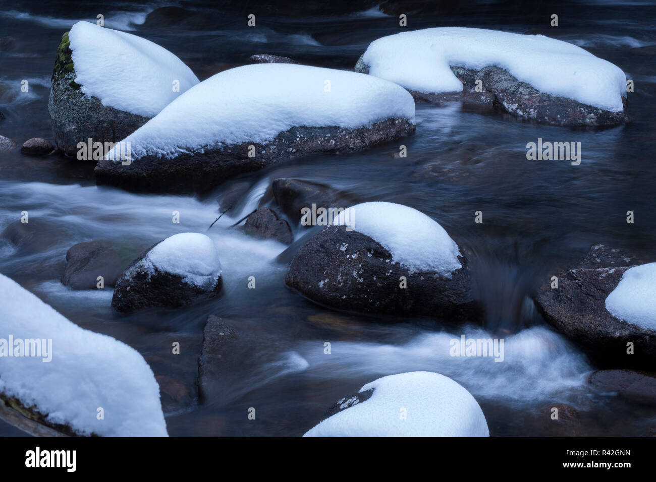 Water flows past snow covered rocks Stock Photo - Alamy